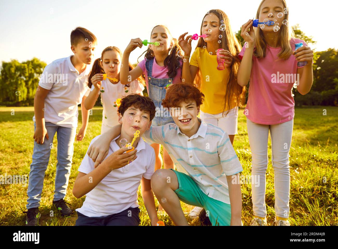 Cheerful happy kids standing on the grass blowing bubbles in summer ...