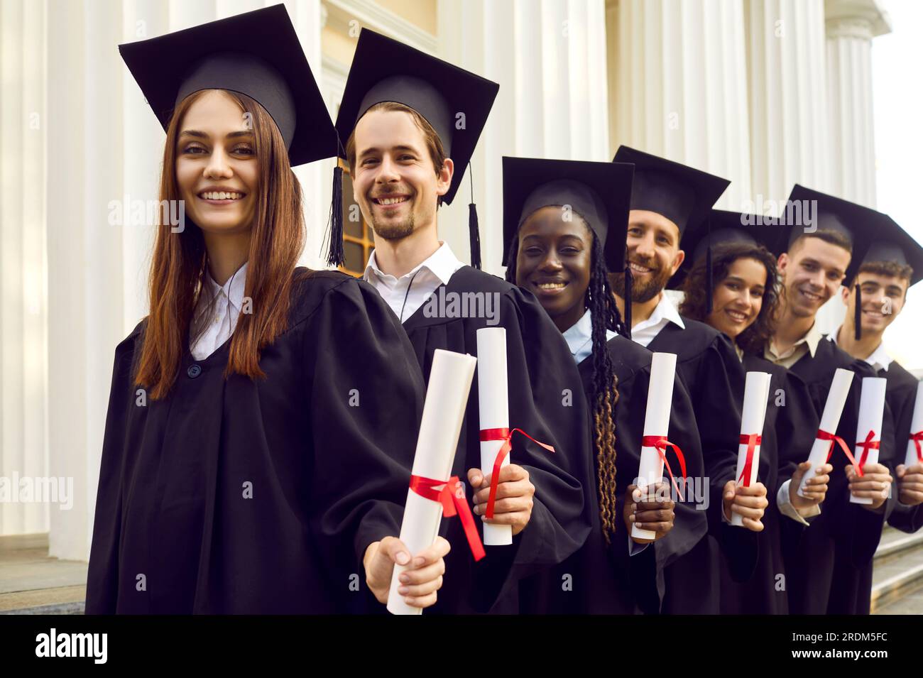 Graduate students standing in a row in black robes with diplomas in ...