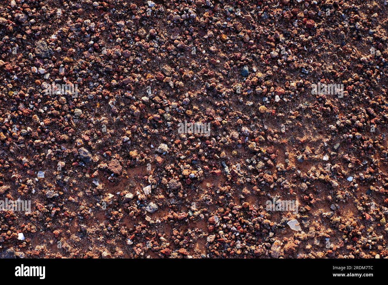 Coarse red metal ore rich gravel and sand, flat surface in hard sunset ...