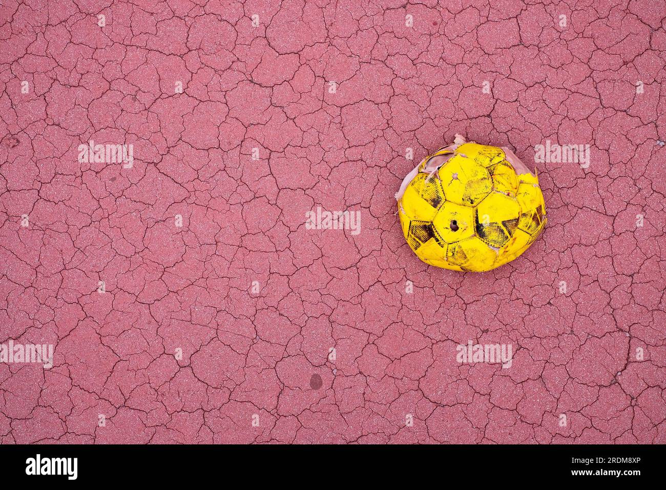 Punctured deflated yellow soccer ball on a red surface, offset with ...