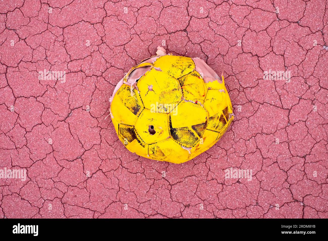 Punctured deflated yellow soccer ball on a red surface, centered and ...