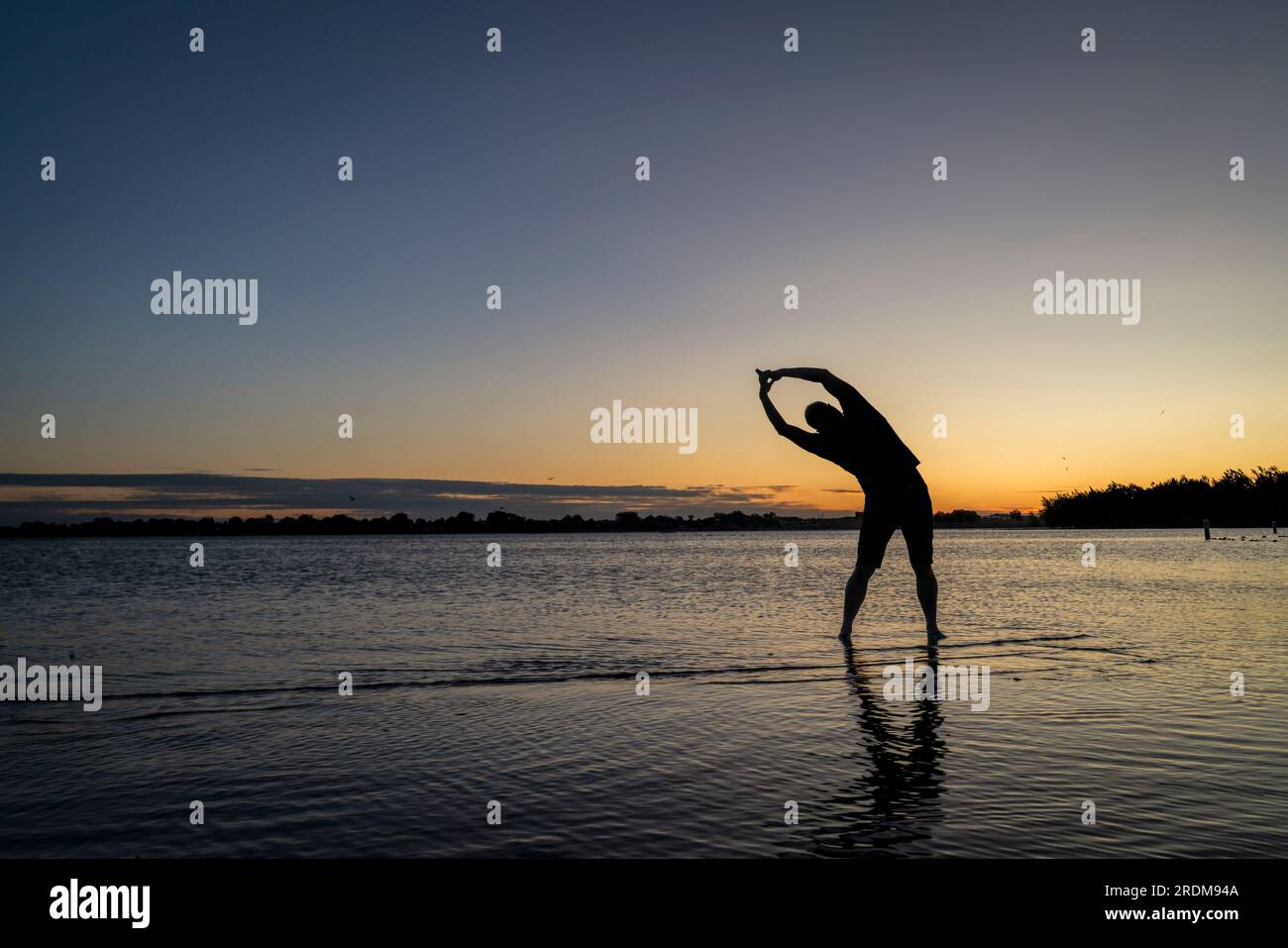 practicing yoga palm tree pose - sunrise silhouette of a man on a lake ...