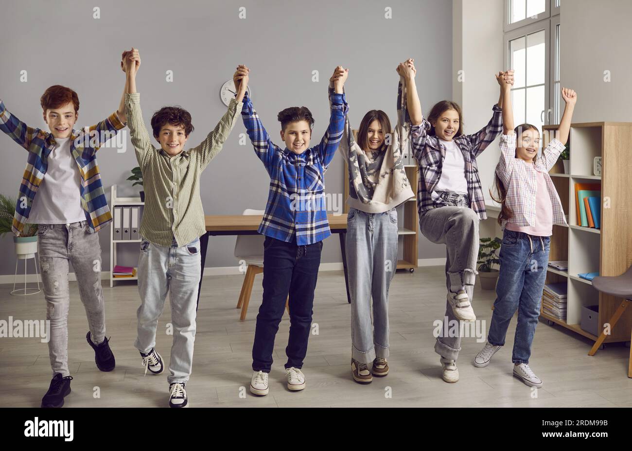 Group of happy junior school students standing with their hands raised ...
