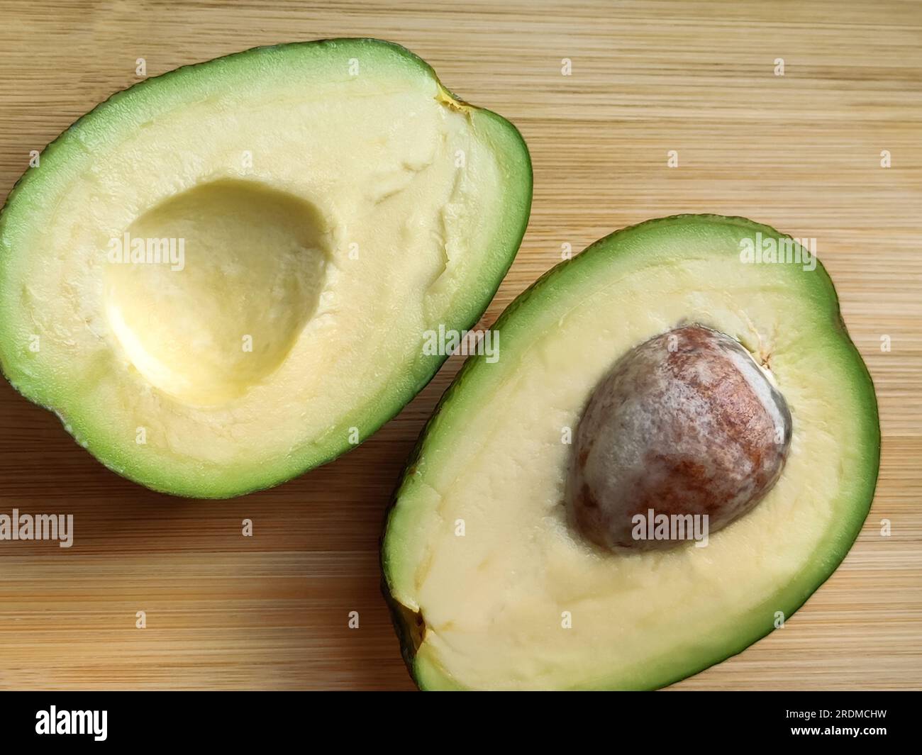 Two slices of avocado on wooden background. Healthy food. Two halves of ...