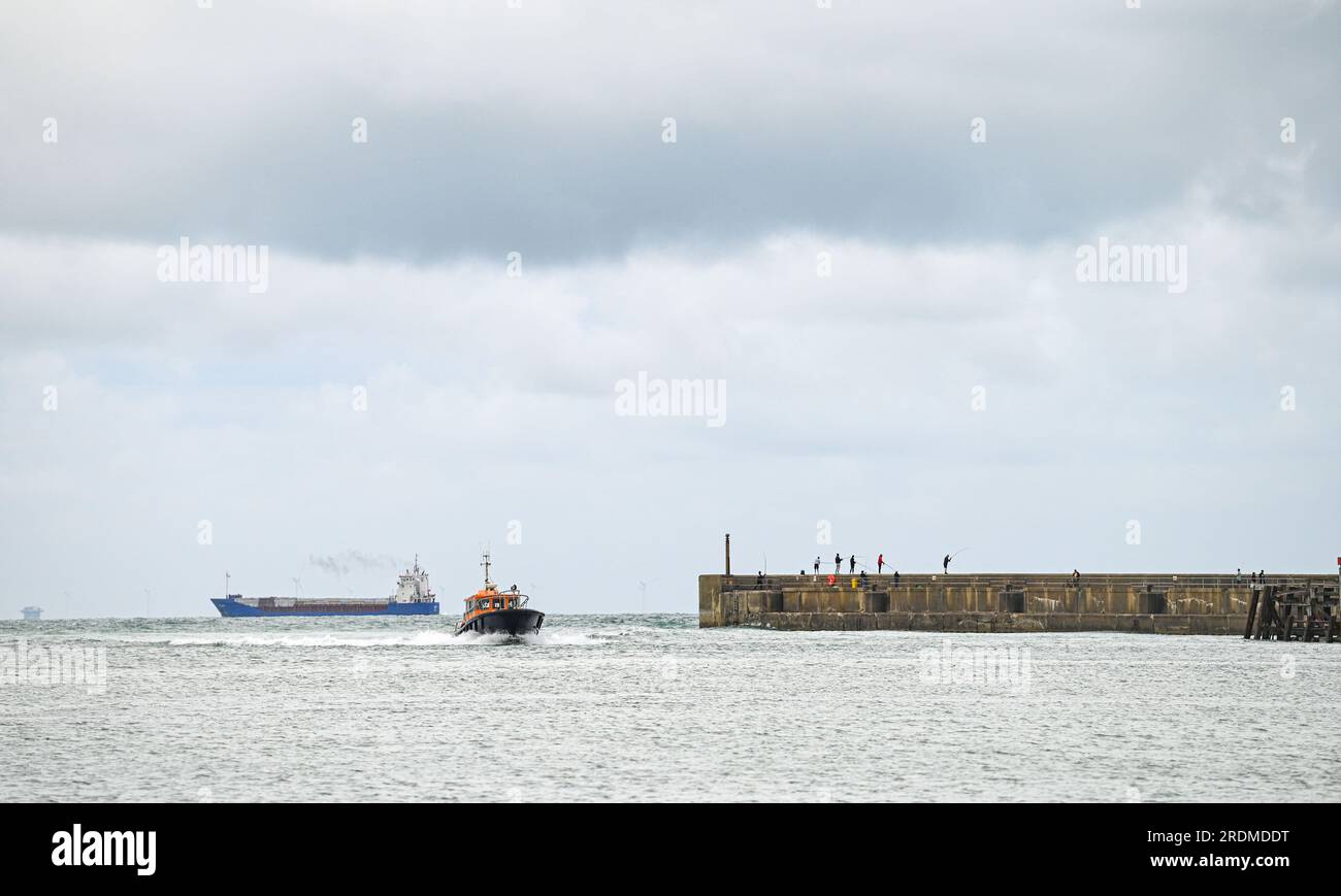 Shoreham Harbour port pilot boat with cargo ship behind and fisherman ...