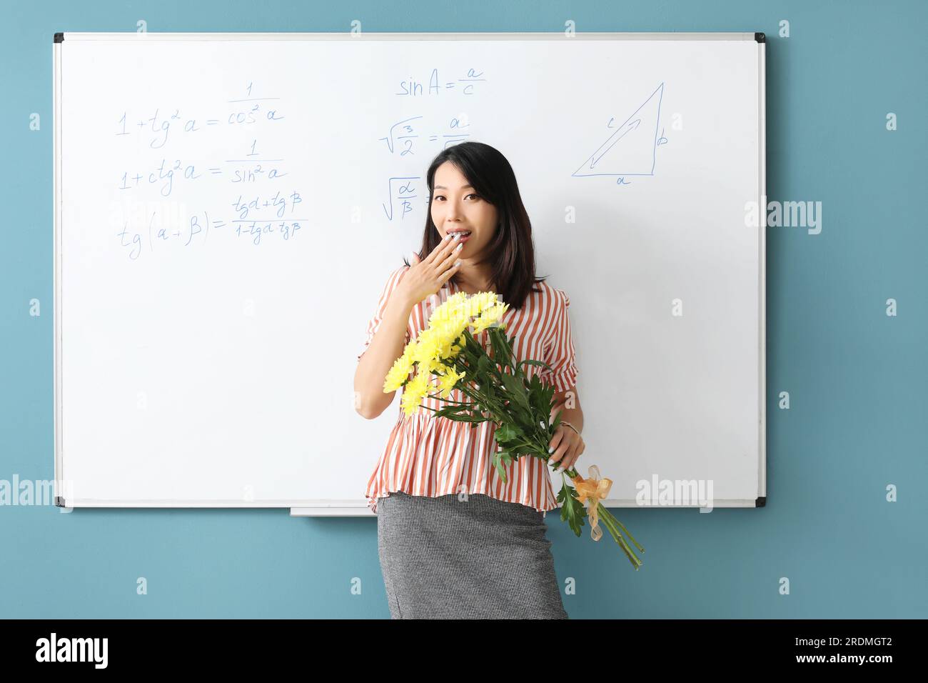 Asian Math teacher with bouquet of flowers near flipboard in classroom ...