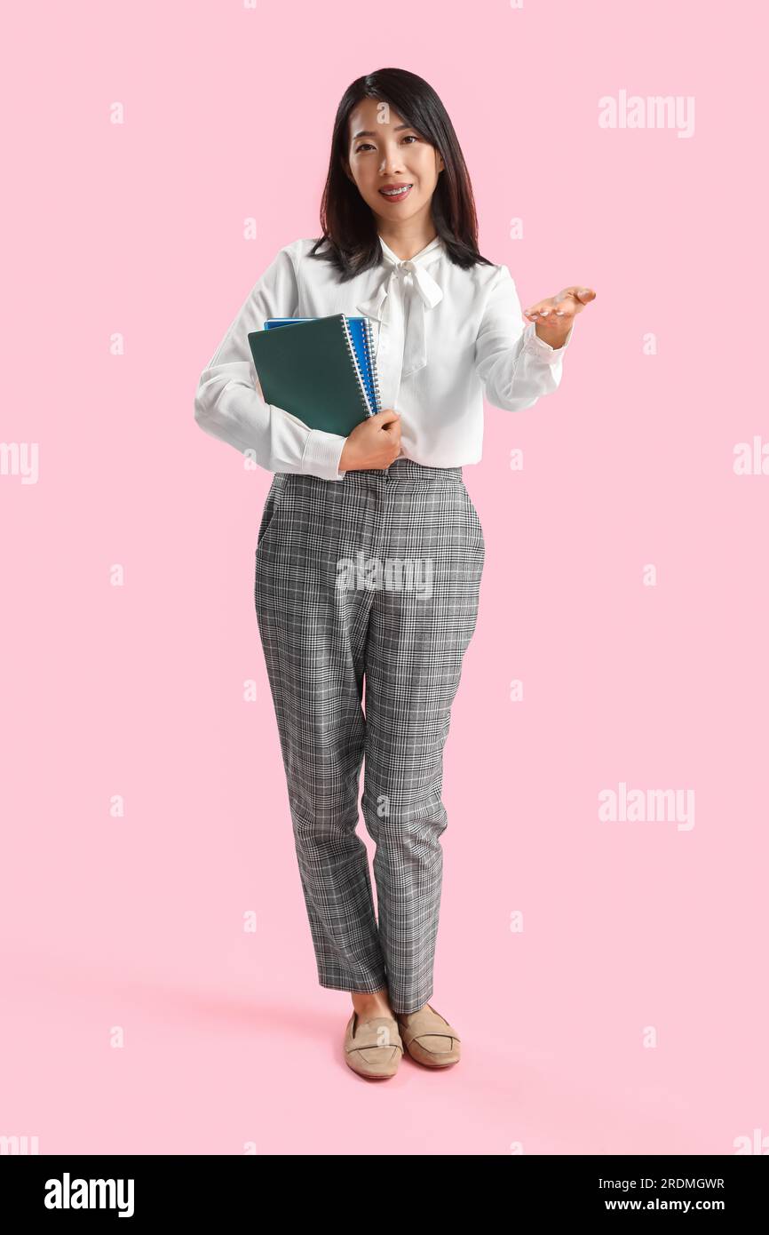 Female Asian teacher with notebooks on pink background Stock Photo - Alamy