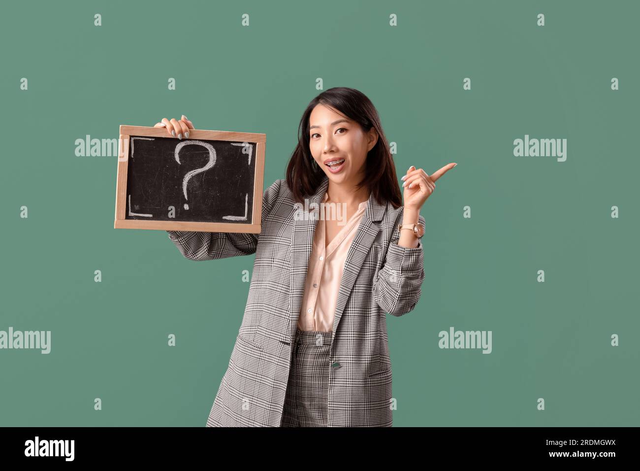 Female Asian teacher holding chalkboard with question mark on green ...