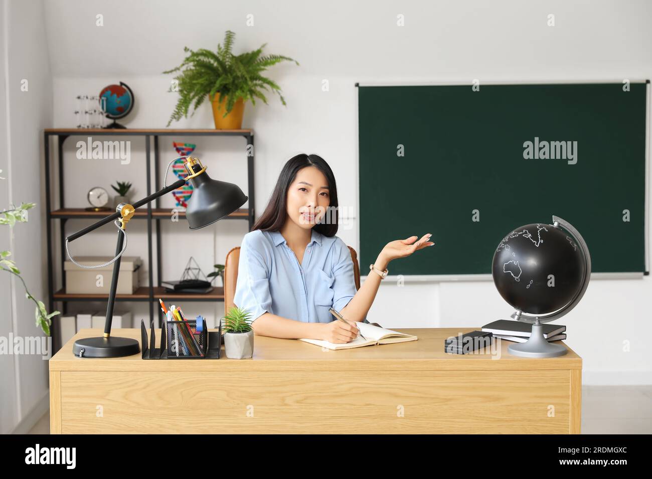 Female Asian teacher sitting at table in classroom Stock Photo - Alamy