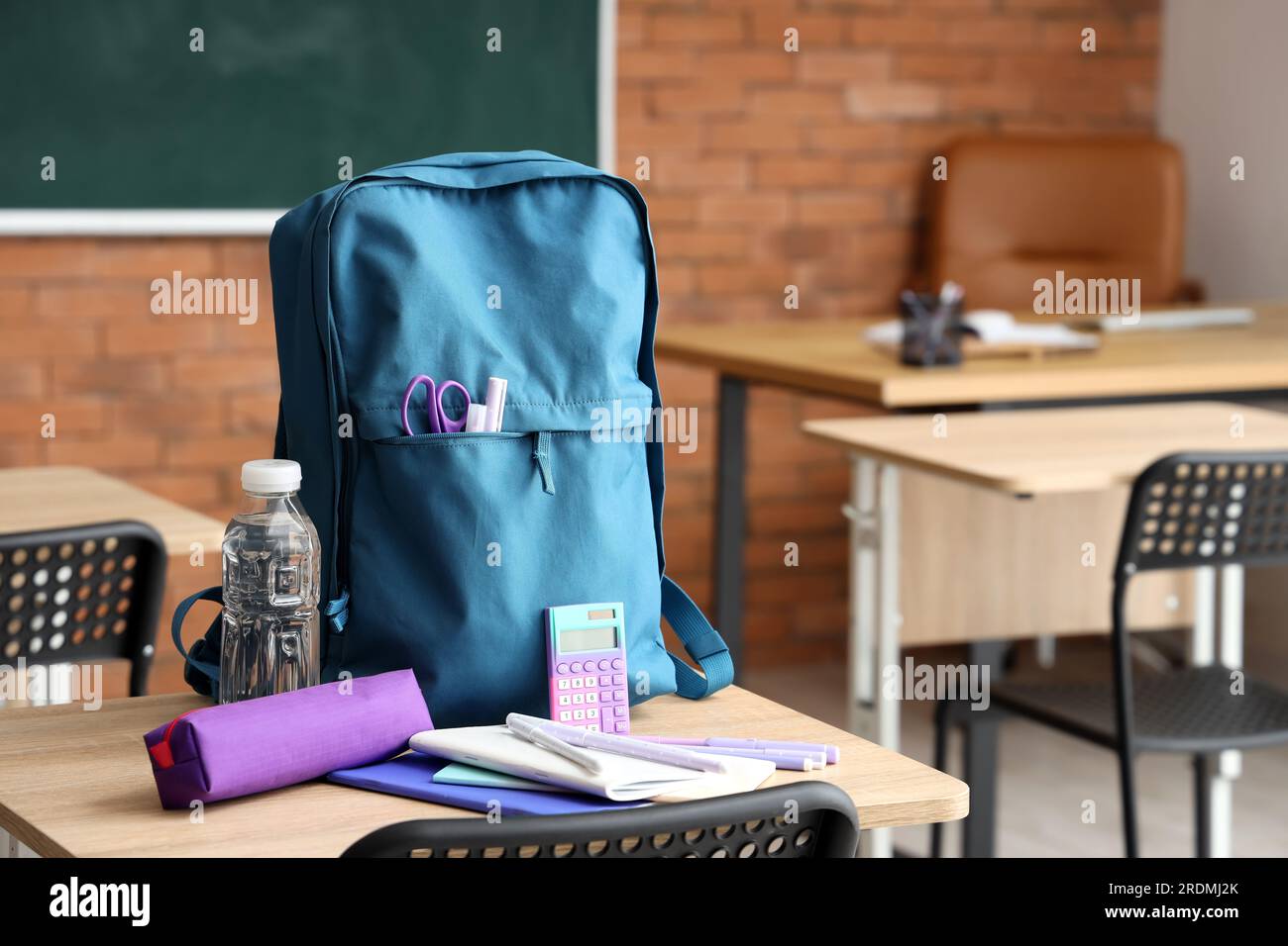 Blue school backpack with stationery and bottle of water on desk in ...