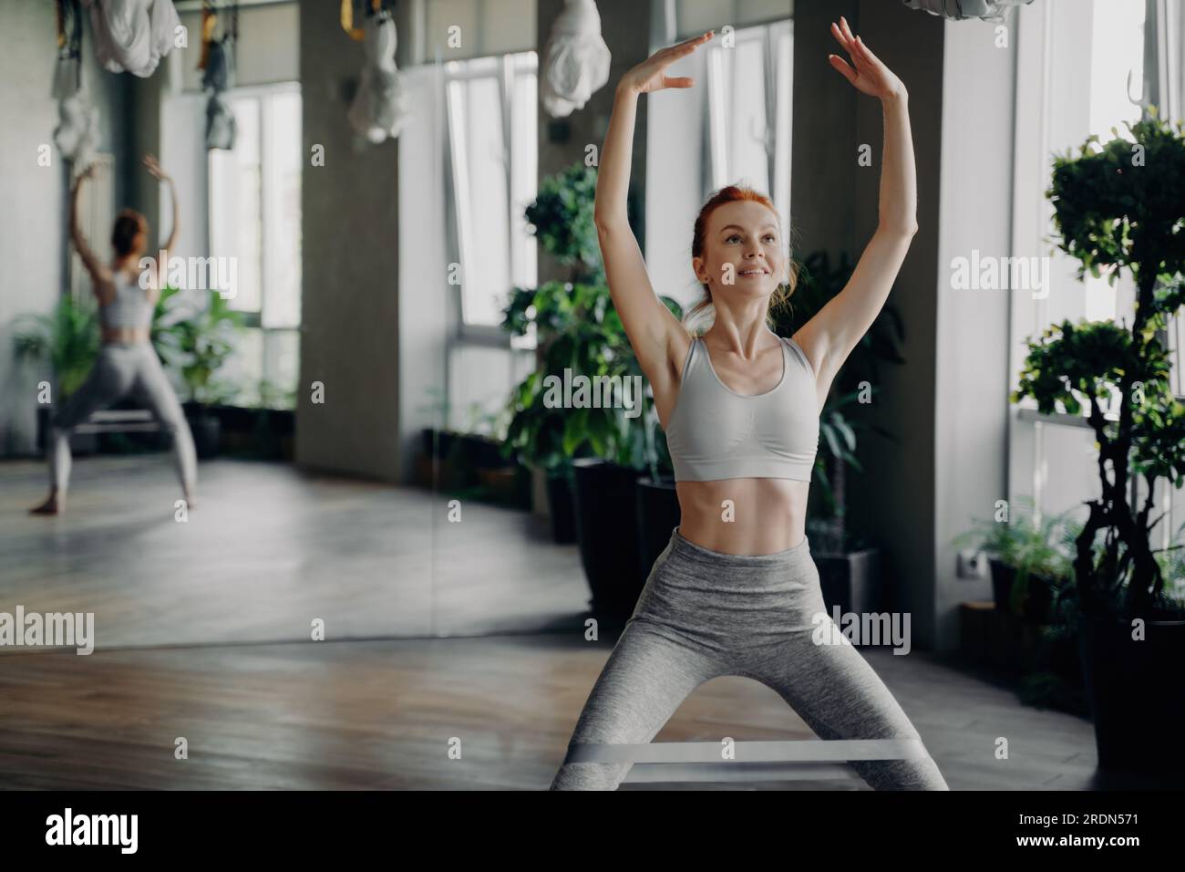 Slender redhead fitness instructor enjoys squats with pilates ...