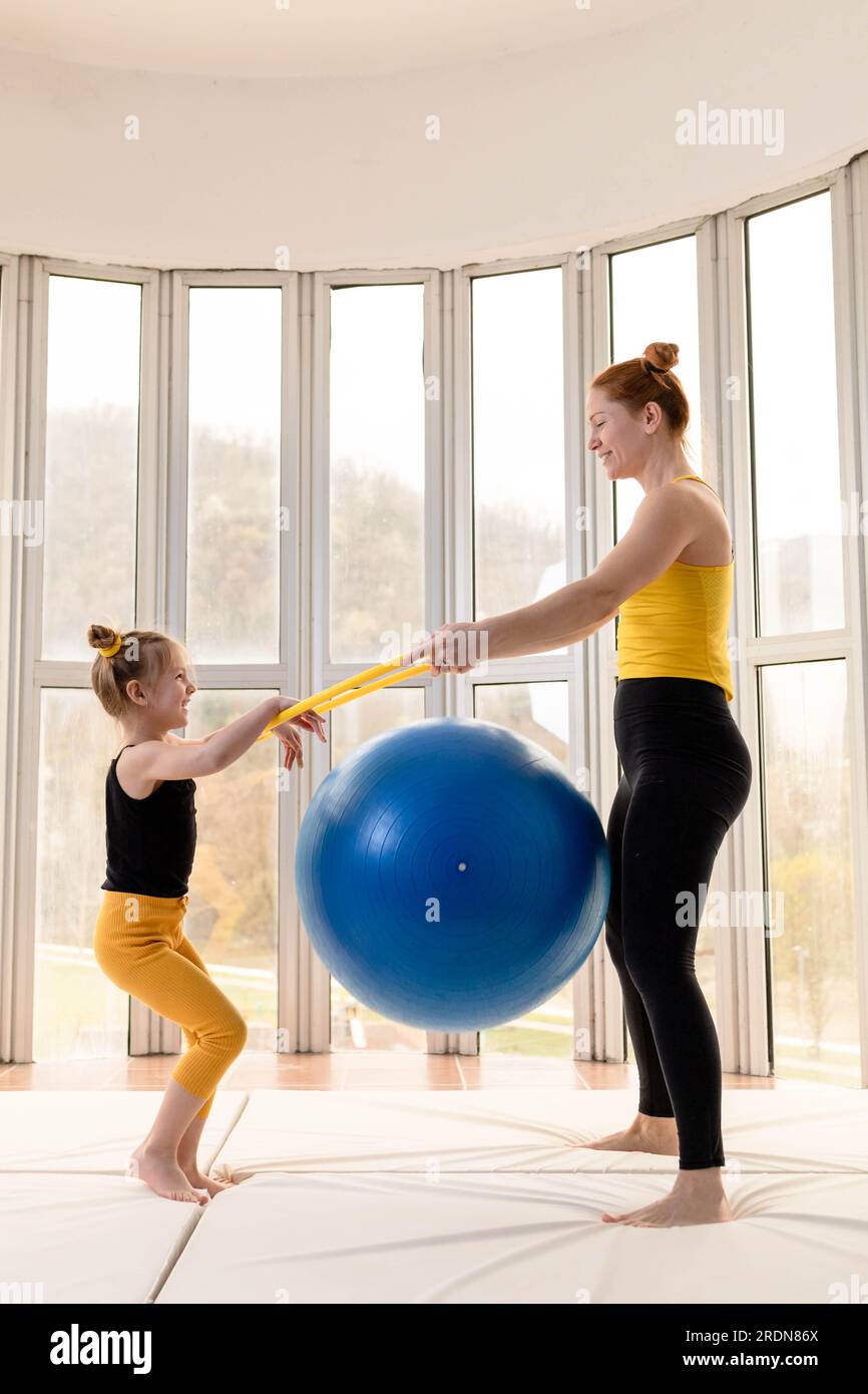 Young fit mom and her daughter having fun with fitness ball in a gym ...