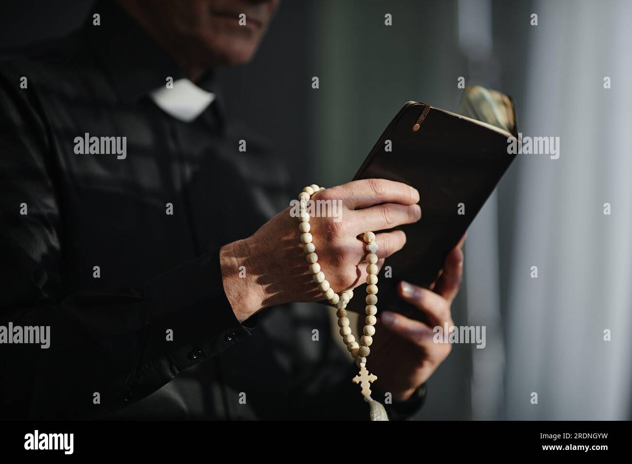 Side view closeup of unrecognizable priest holding Bible and rosary ...