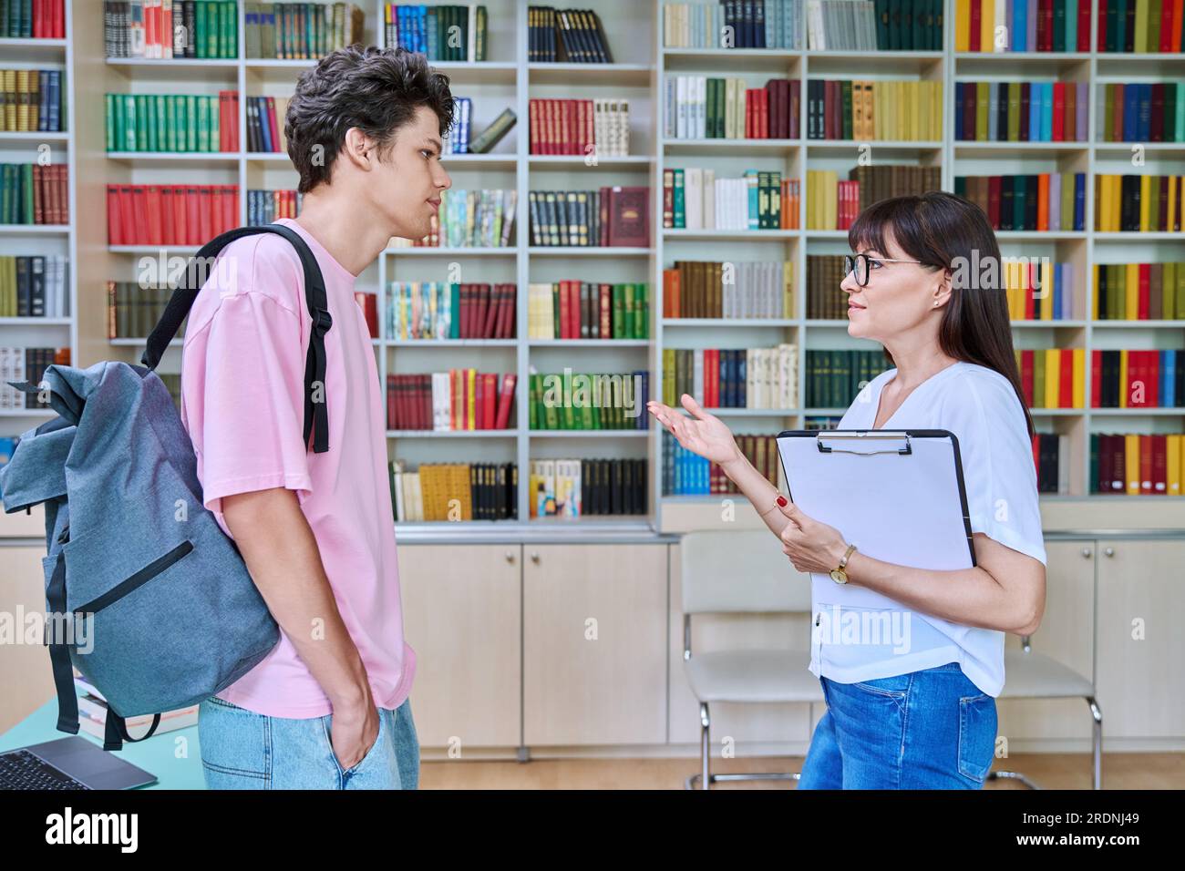 Middle-aged female teacher talking to male college student inside library Stock Photo - Alamy