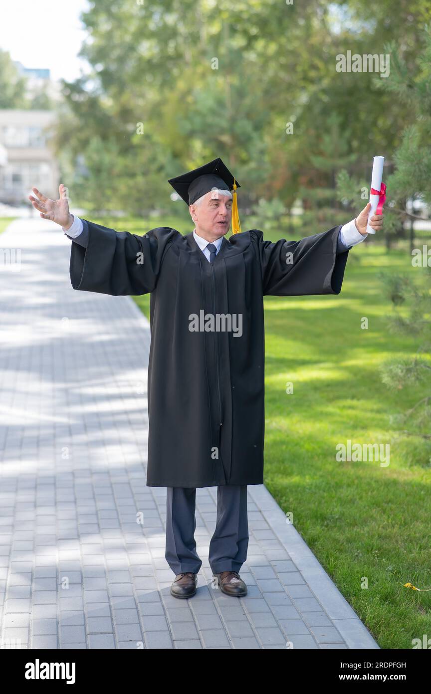 An elderly gray-haired man in a graduate robe spread his arms to the ...