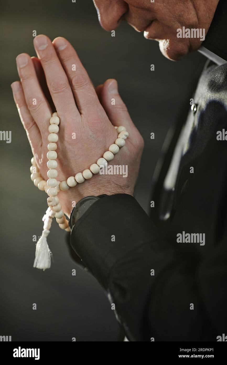 Vertical side view portrait of senior priest with hands clasped in ...