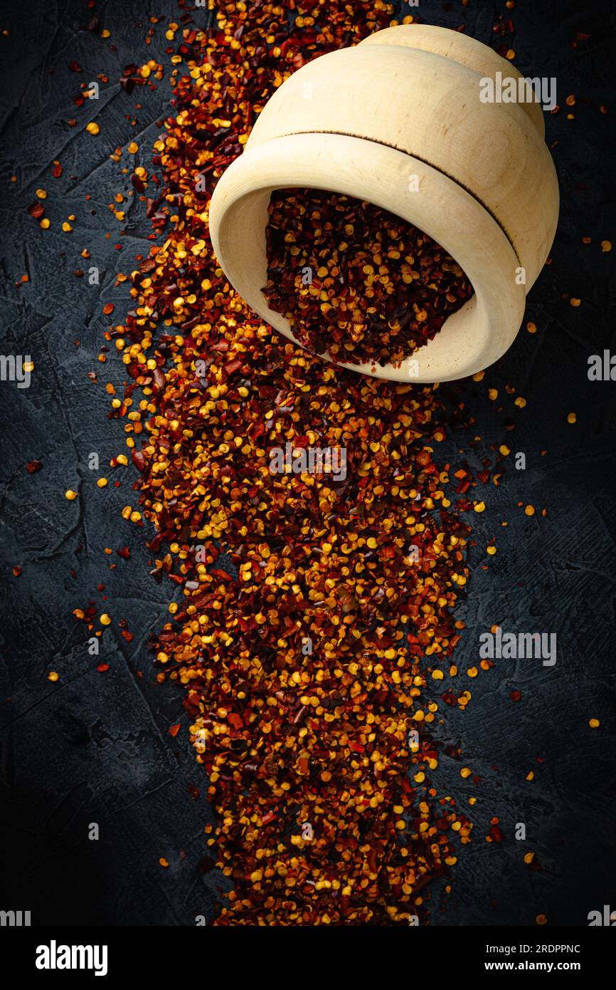 Dried red pepper flakes in a wooden bowl. Chili pepper flakes on a dark ...