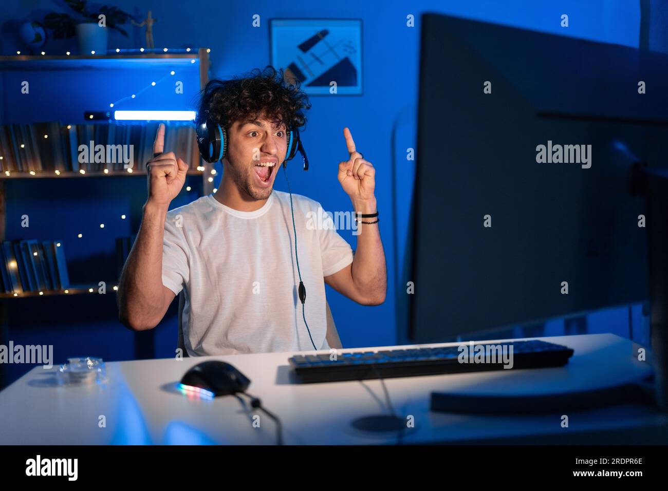 Surprised young arabic gamer wearing headphones playing video game on ...