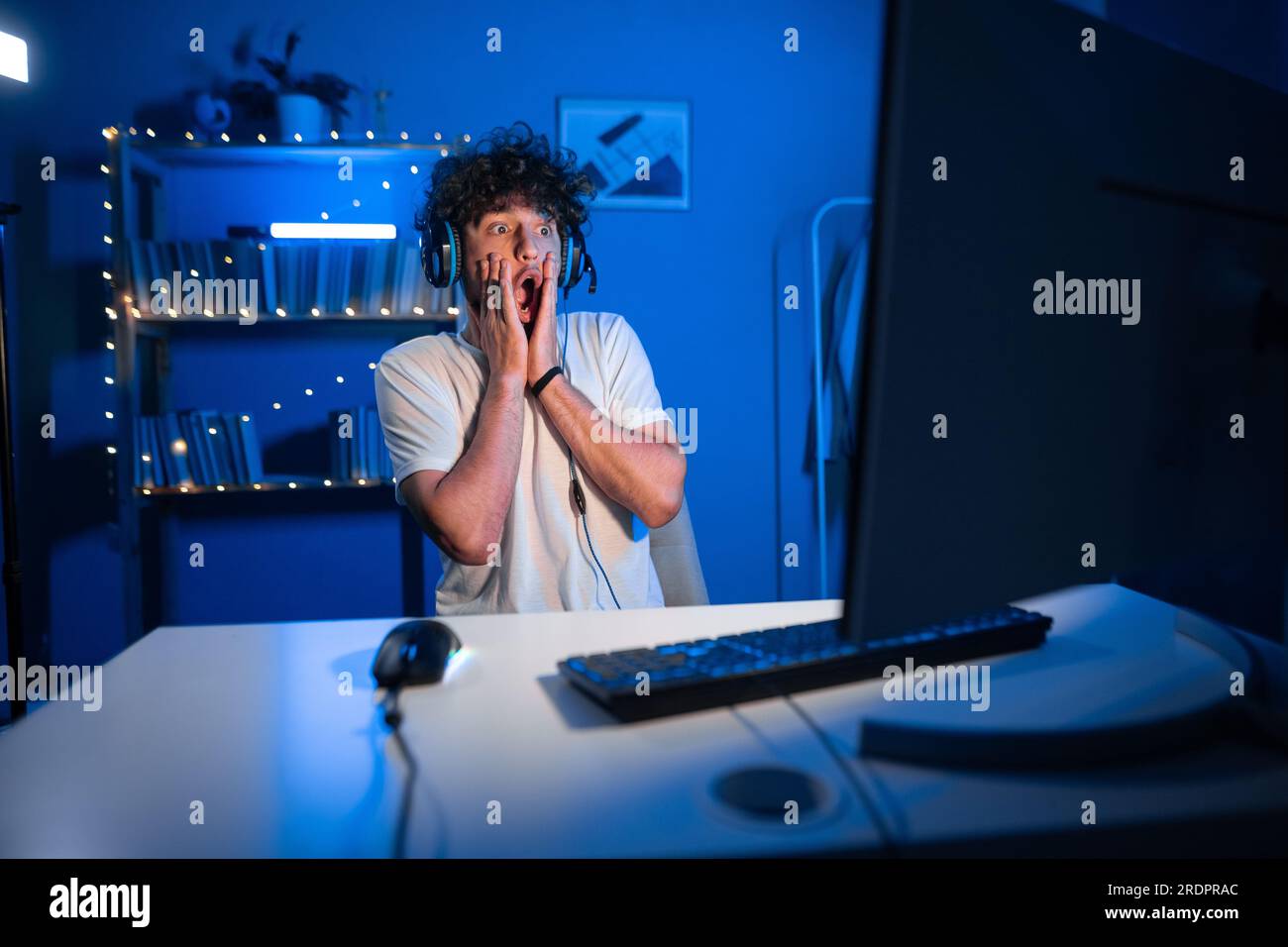 Shocked arabic gamer in headset at night near computer staring at ...
