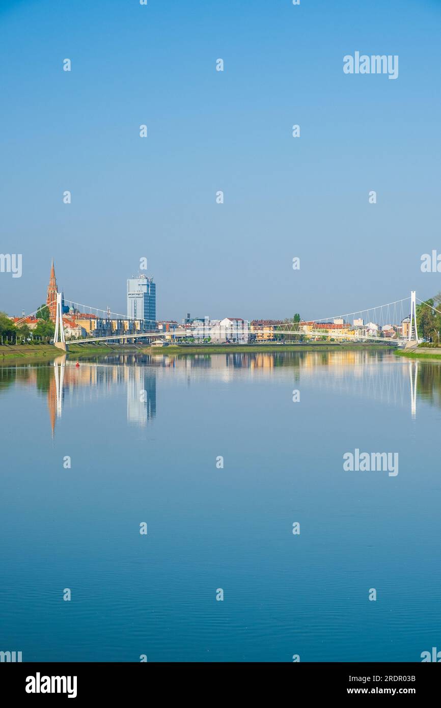 Pedestrian bridge over the Drava river and skyline of city of Osijek ...