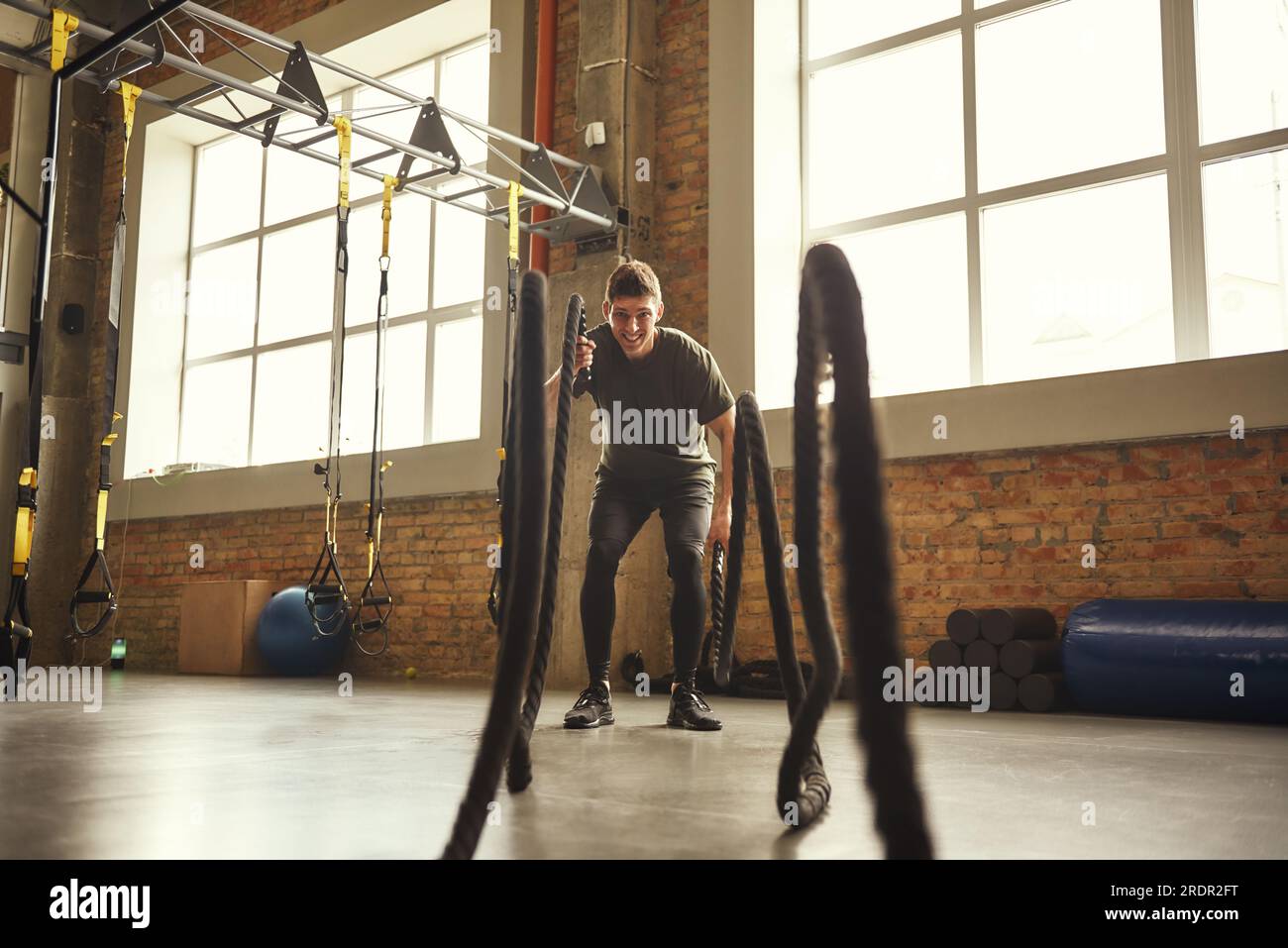 Battle ropes exercises. Young and strong man doing CrossFit exercises ...