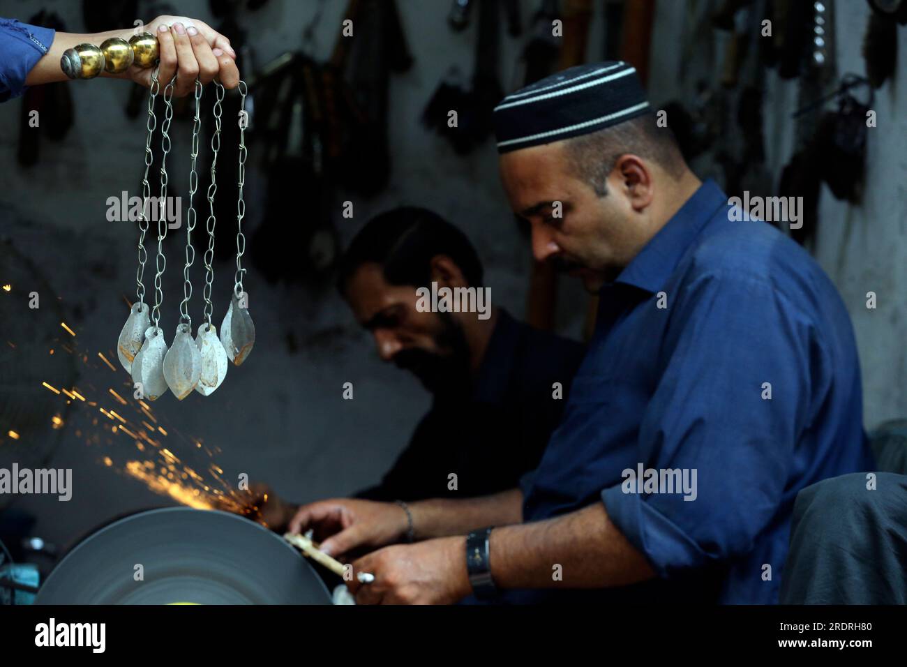 A Pakistani iron smith sharpens knives, as bunches of knives and chains ...