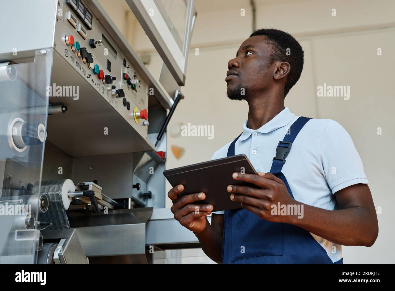 Side view of African American factory worker holding tablet while ...