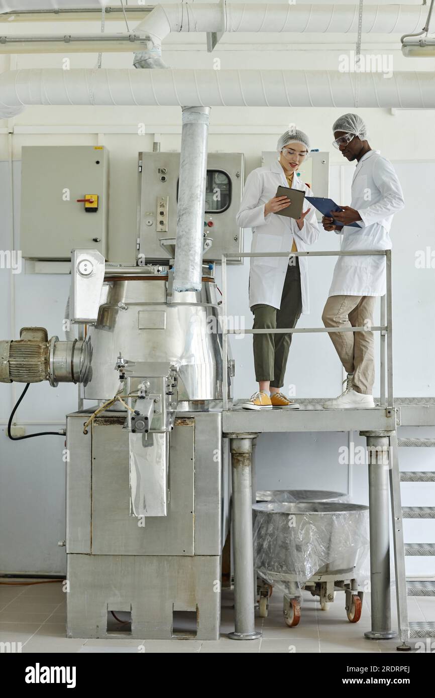 Vertical full length shot of two workers wearing lab coats using laptop ...