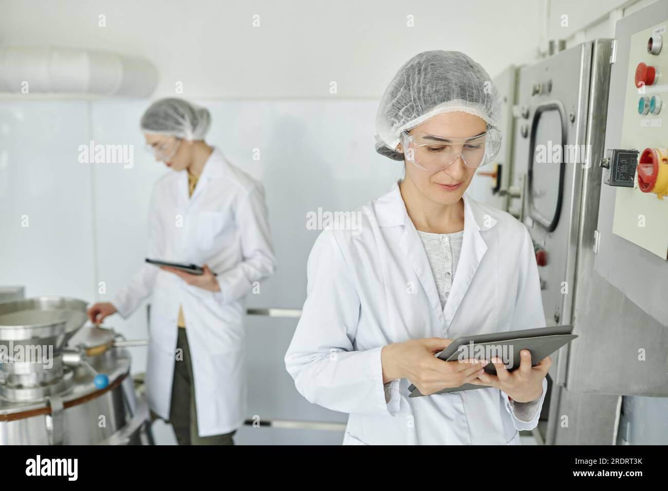 Portrait of two women wearing lab coats working at factory in food or ...