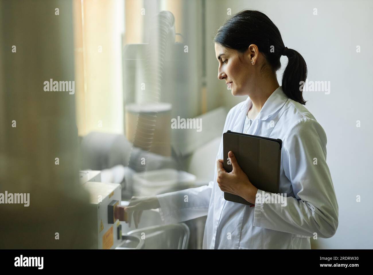Side view portrait of adult woman wearing lab coat using equipment in ...