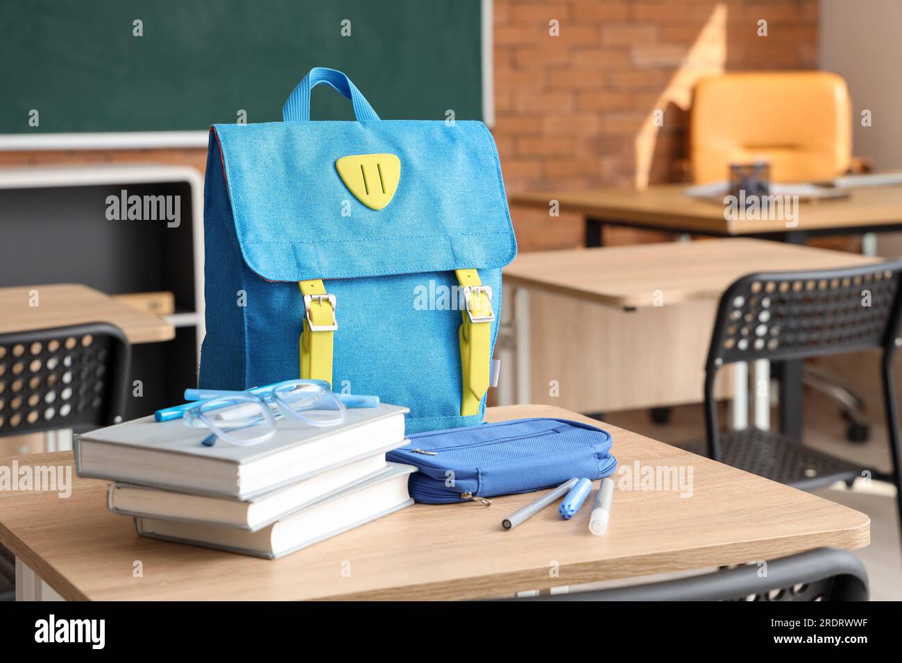Blue school backpack with stationery and eyeglasses on desk in ...