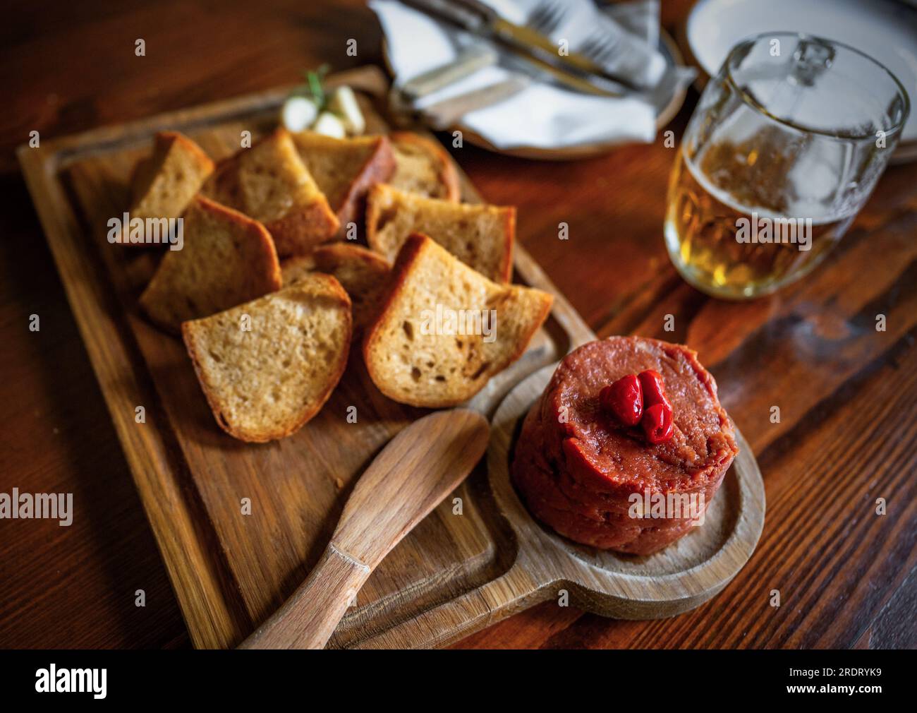 Wooden table with tartar steak and toasts on board, plate, cutlery and ...