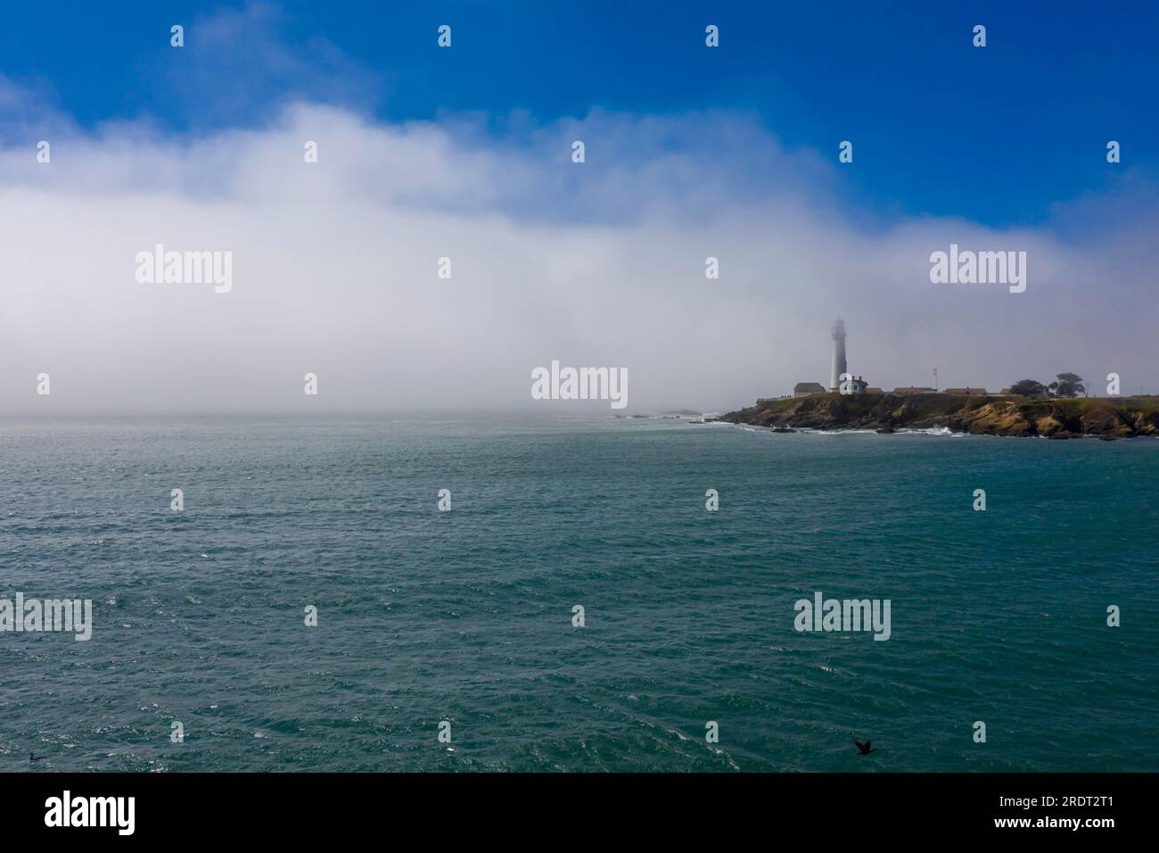 Aerial view of a lighthouse off the California Coast as fog settles in ...
