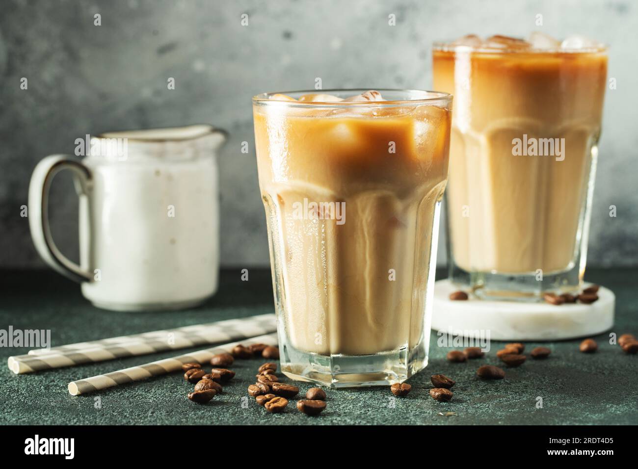 Ice coffee in a tall glass with cream poured over, ice cubes and beans ...