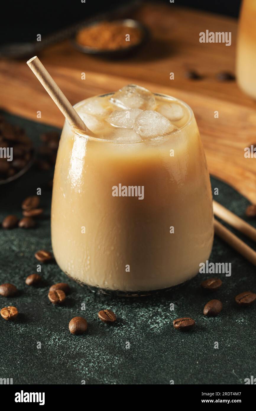 Ice coffee in a tall glass with cream poured over, ice cubes and beans ...