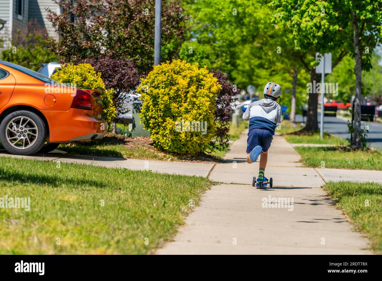 A child rides his scooter down a sidewalk in a suburban environment ...