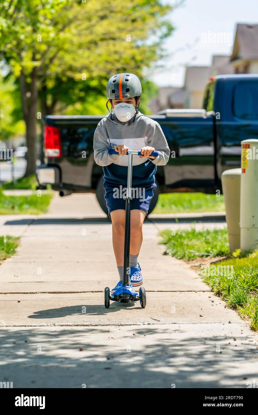 A child rides his scooter down a sidewalk in a suburban environment ...