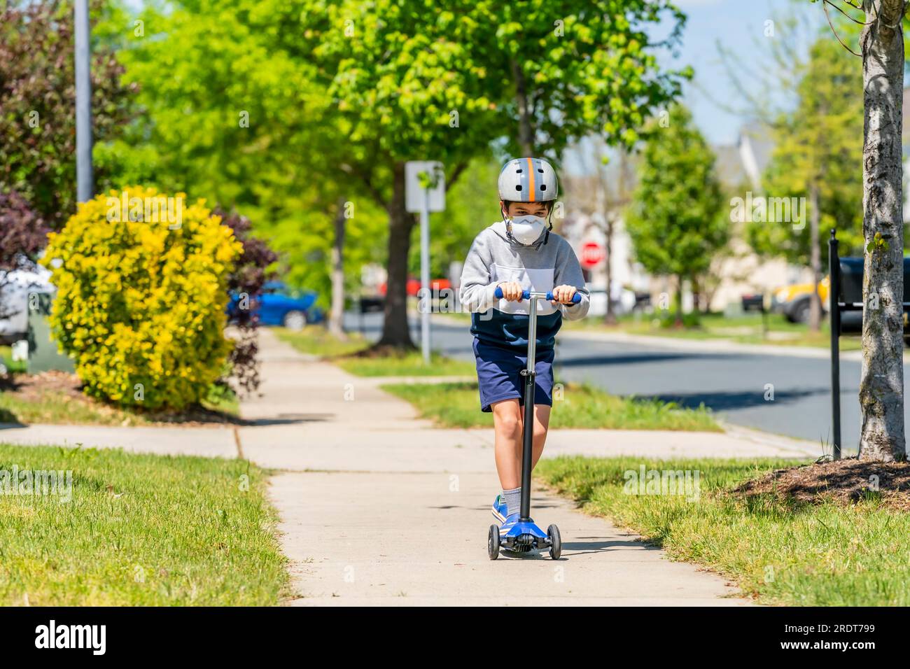 A child rides his scooter down a sidewalk in a suburban environment ...
