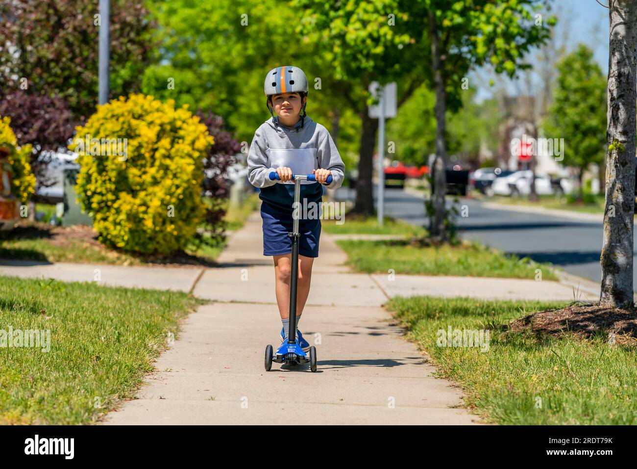 A child rides his scooter down a sidewalk in a suburban environment ...