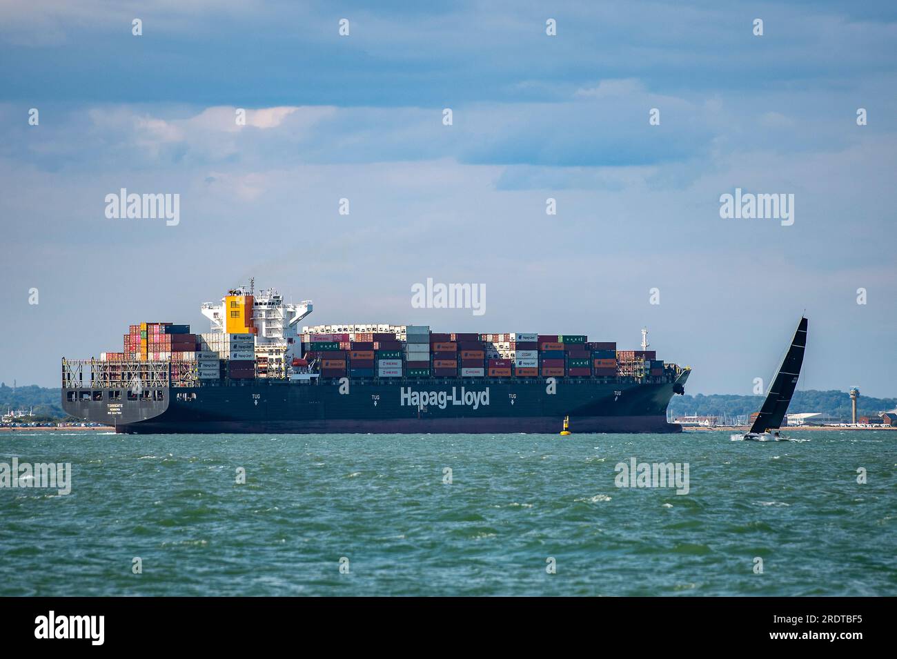 large container ship passing racing yacht in the solent off of cowes ...
