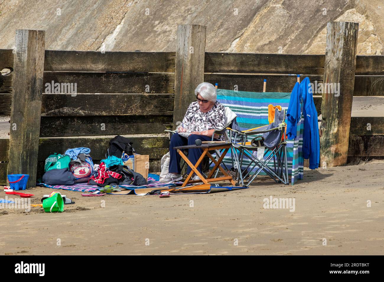 older lady taking it easy sitting in a chair behind a windbreak on the ...