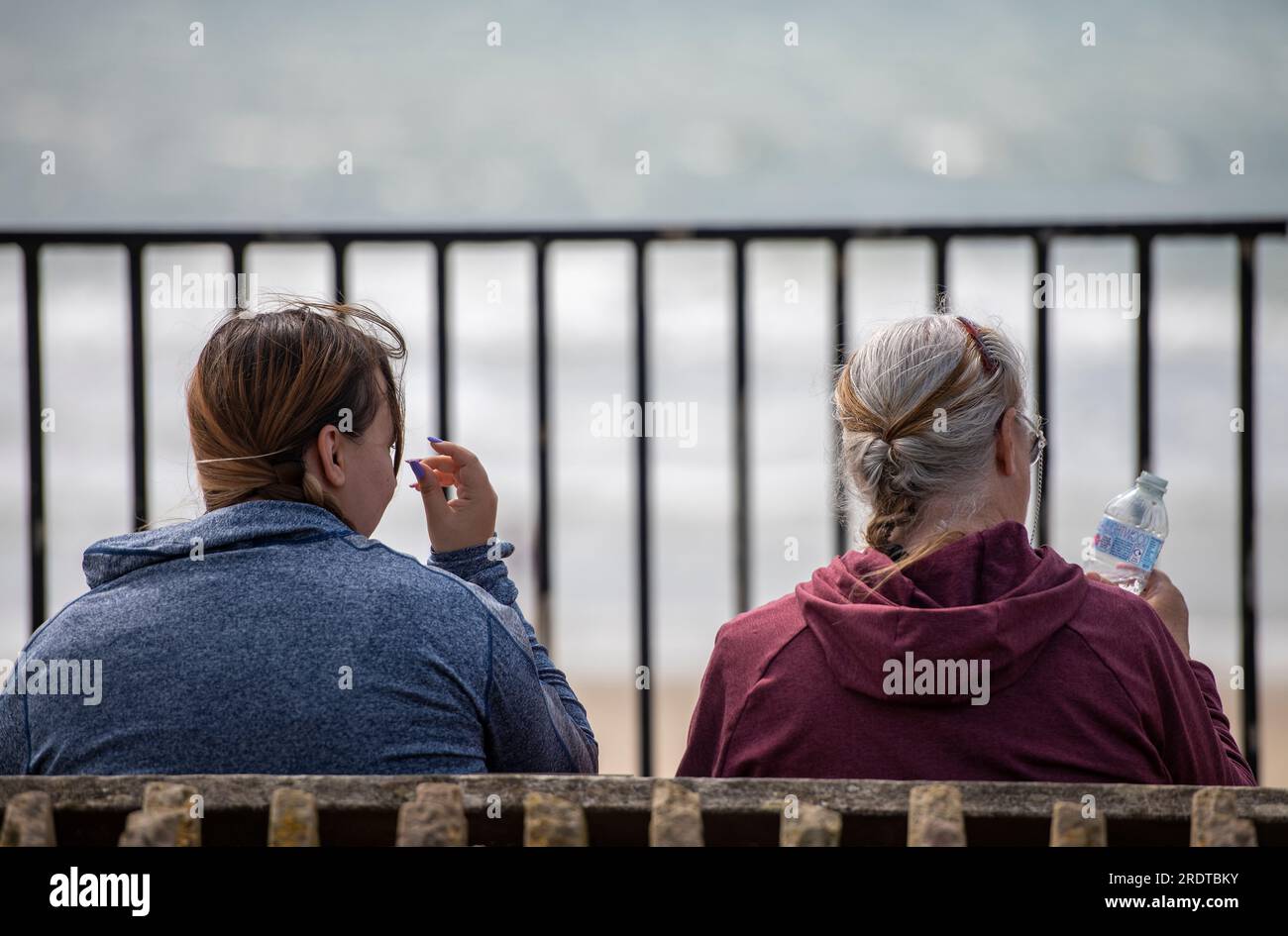 two older ladies sitting on a bench at the seaside relaxing and talking ...