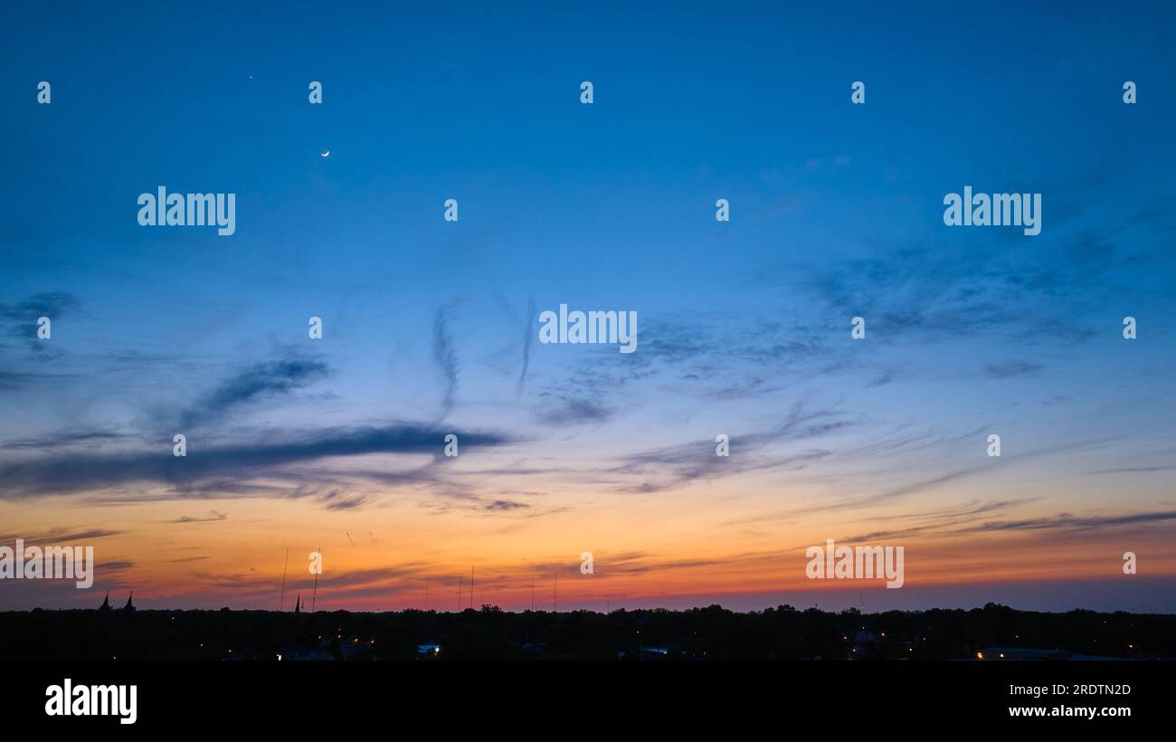 Crescent moon in glowing dusk sky fading to blue with dark horizon ...