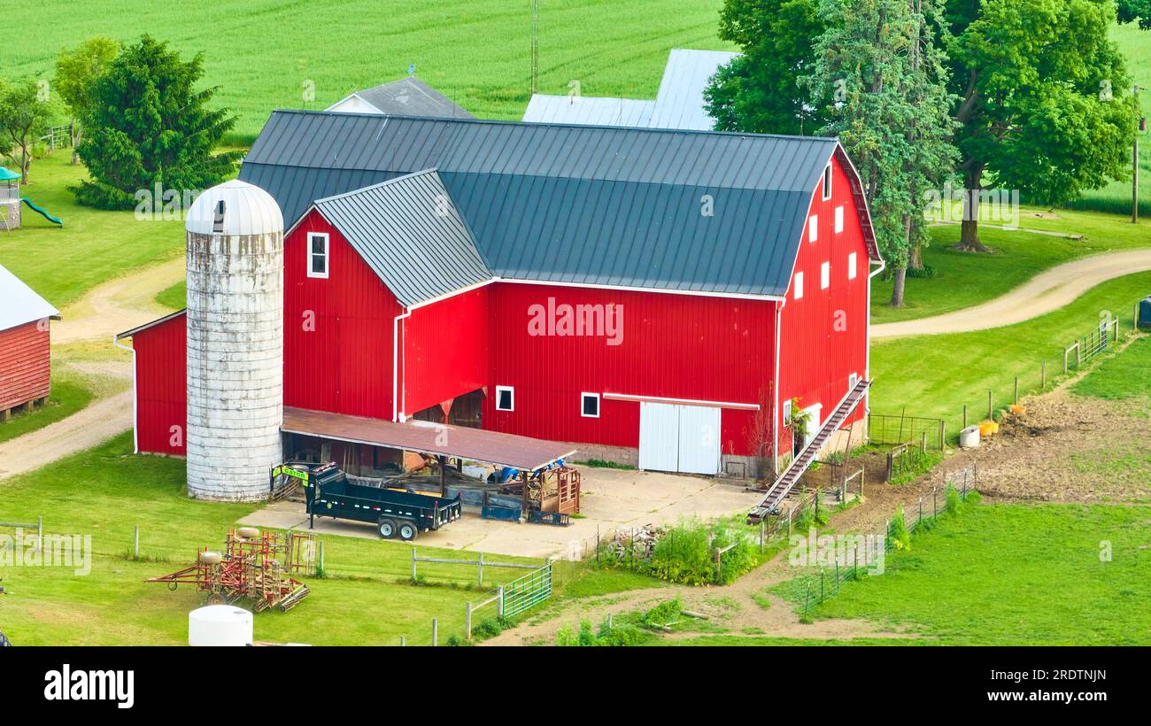 Aerial red barn with white silo and trailer parked out front in summer ...