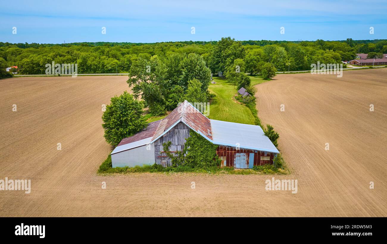Old rusty barn in center with empty dirt farmland on three sides and a ...