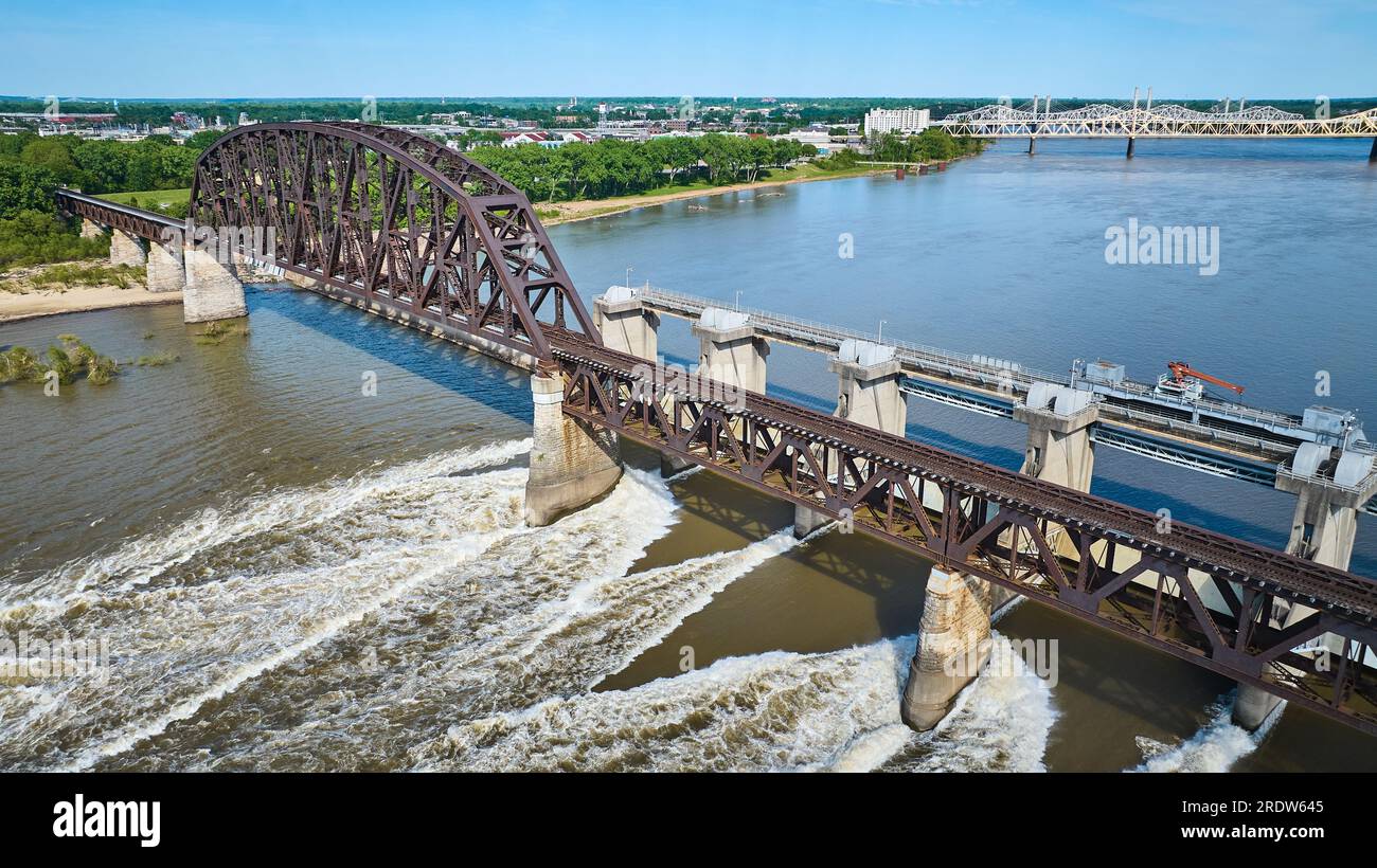 Brown truss railroad bridge over large dam aerial with distant shore ...