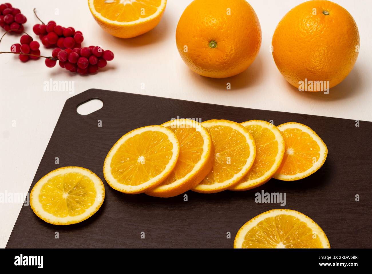 Slicing an orange on a cutting board. Two whole oranges. White ...
