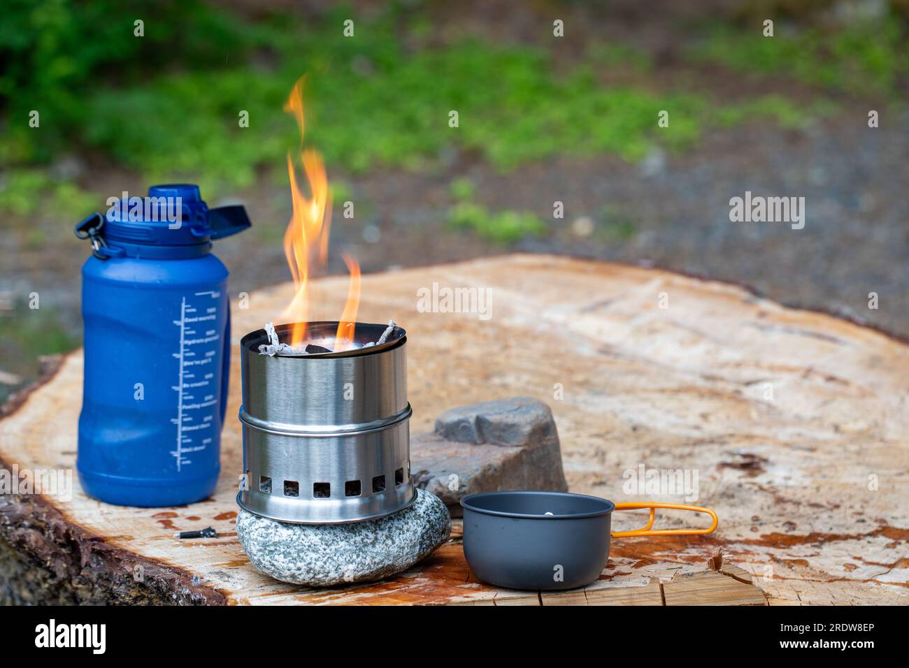 Fire in a portable camp stove and collapsable water bottle and cup on a ...