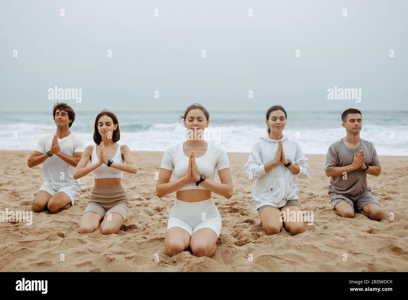 Youth practising yoga on the ocean's edge, zen friends men and women ...