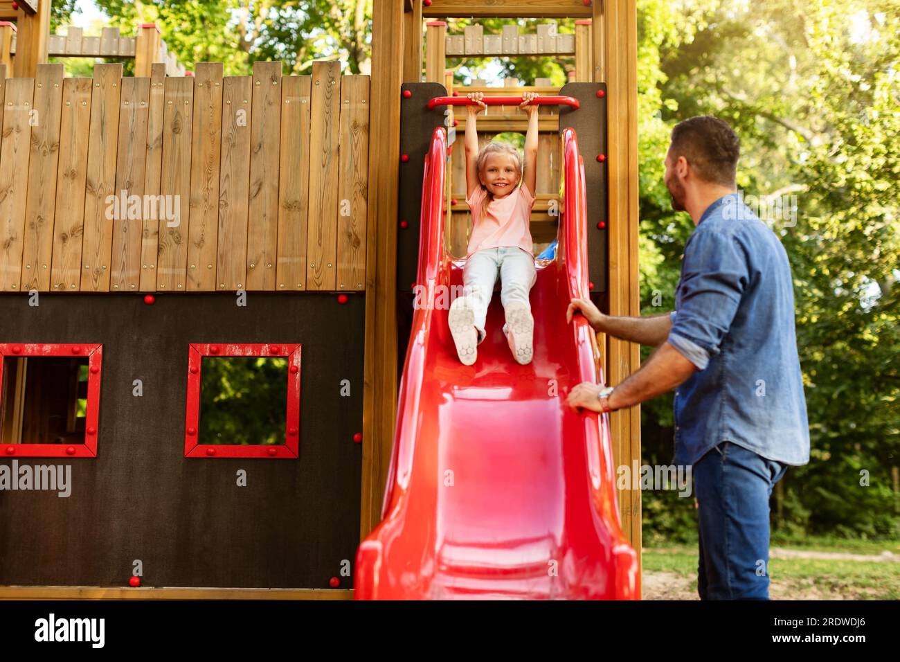 Handsome dad catching daughter, girl riding on slide at modern ...